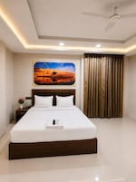 Quarto de hotel com uma cama grande, um ventilador de teto, uma mesa de cabeceira com um vaso e uma pintura acima da cama.