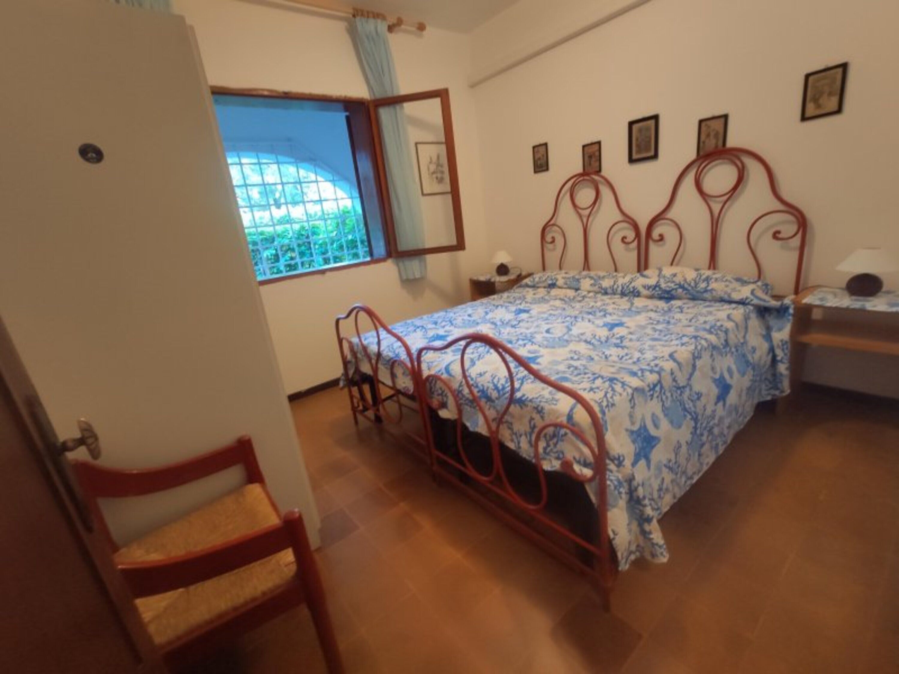 Um quarto com cama, cadeira, janela e parede decorada com quadros.