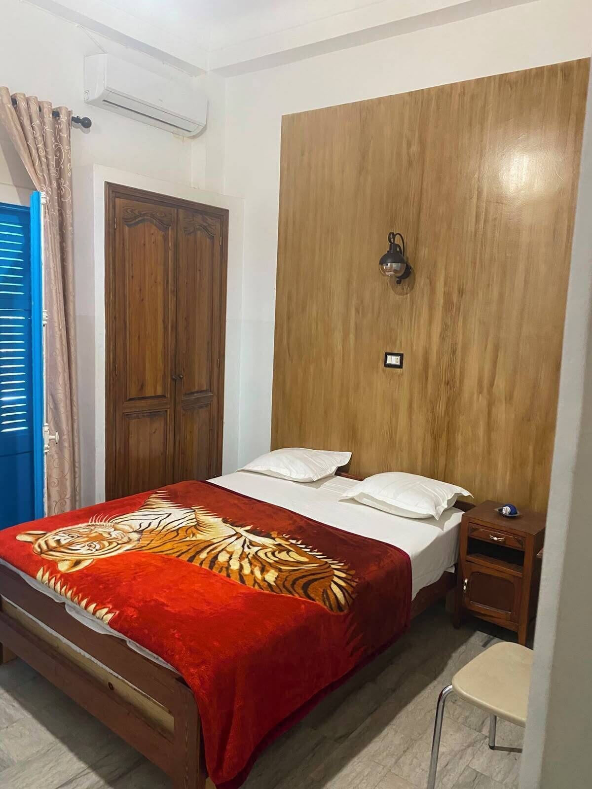 Quarto com cama, guarda-roupa de madeira, mesa de cabeceira e luminária na parede.