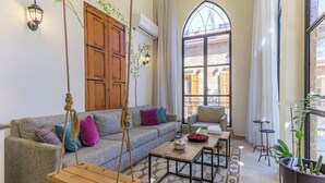 Uma sala de estar com sofá, balanço, mesa de centro e vista da rua por grandes janelas.