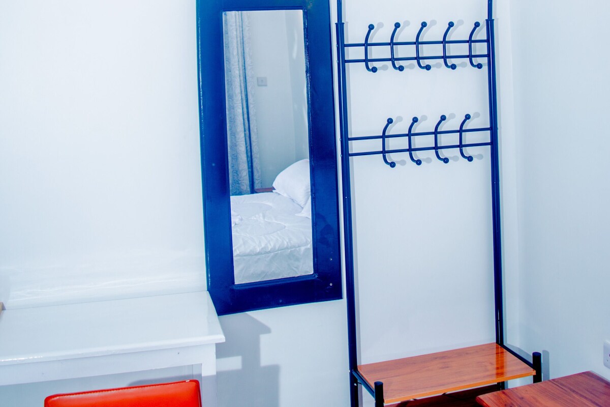 Quarto com cama, espelho, estante de metal, cadeira vermelha e mesa de madeira.