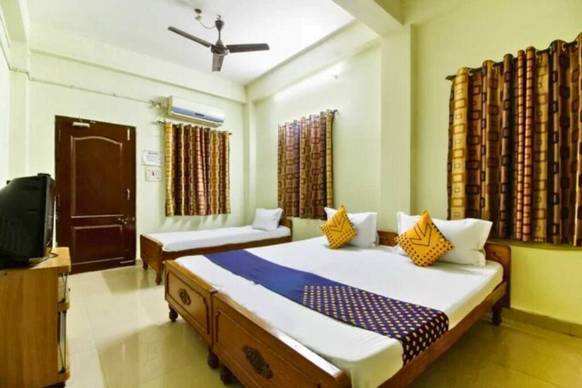 Quarto de hotel com uma cama grande, duas camas menores, um ventilador de teto e cortinas.