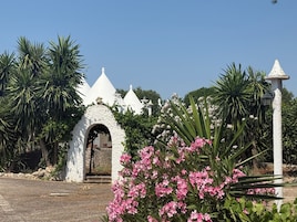 Um edifício branco com arco de pedra, rodeado por vegetação exuberante e flores cor-de-rosa.