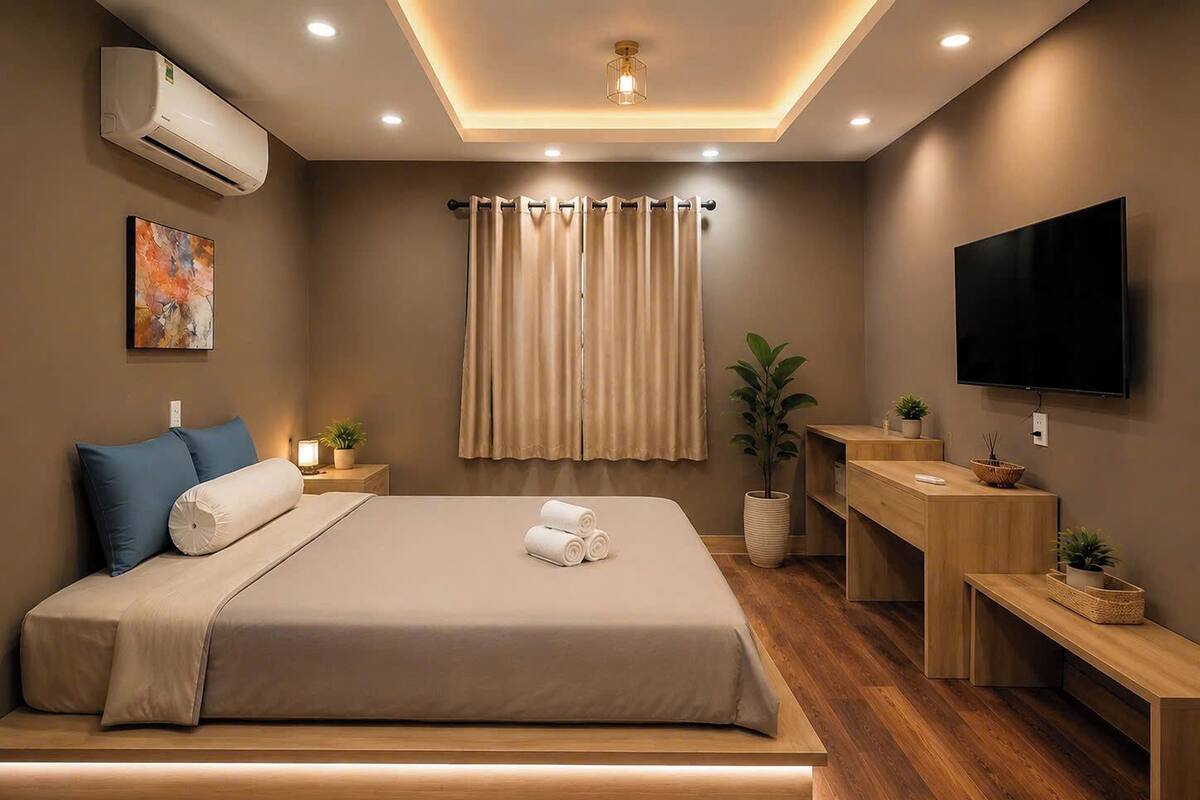 Quarto moderno com cama, mesas de cabeceira, televisão e área de banheiro.