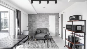 Uma sala de estar moderna com um sofá cinzento, uma mesa de jantar e uma cozinha com micro-ondas e forno em uma prateleira.