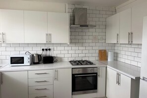 Uma cozinha com armários brancos, micro-ondas, torradeira, chaleira, fogão a gás e forno.