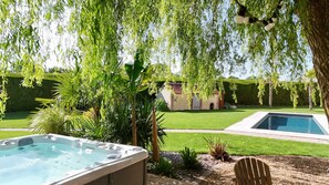 Uma banheira de hidromassagem, uma piscina e um jardim com árvores e uma estrutura de tijolos.
