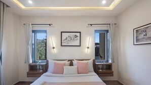 Quarto de hotel moderno com uma cama grande, duas mesas de cabeceira, uma luminária no teto, uma obra de arte emoldurada e uma janela com cortinas.