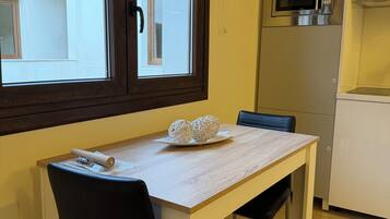 Uma cozinha pequena com micro-ondas, uma mesa com cadeiras e uma janela com vista para prédios.