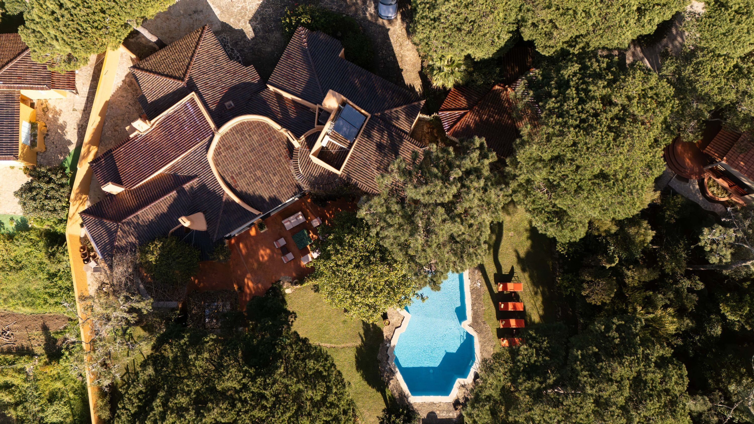 Vista aérea de uma propriedade residencial com piscina, várias áreas cobertas e vegetação ao redor.
