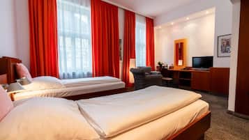 Quarto de hotel com duas camas, uma escrivaninha, uma cadeira, televisão e uma janela grande com cortinas vermelhas.