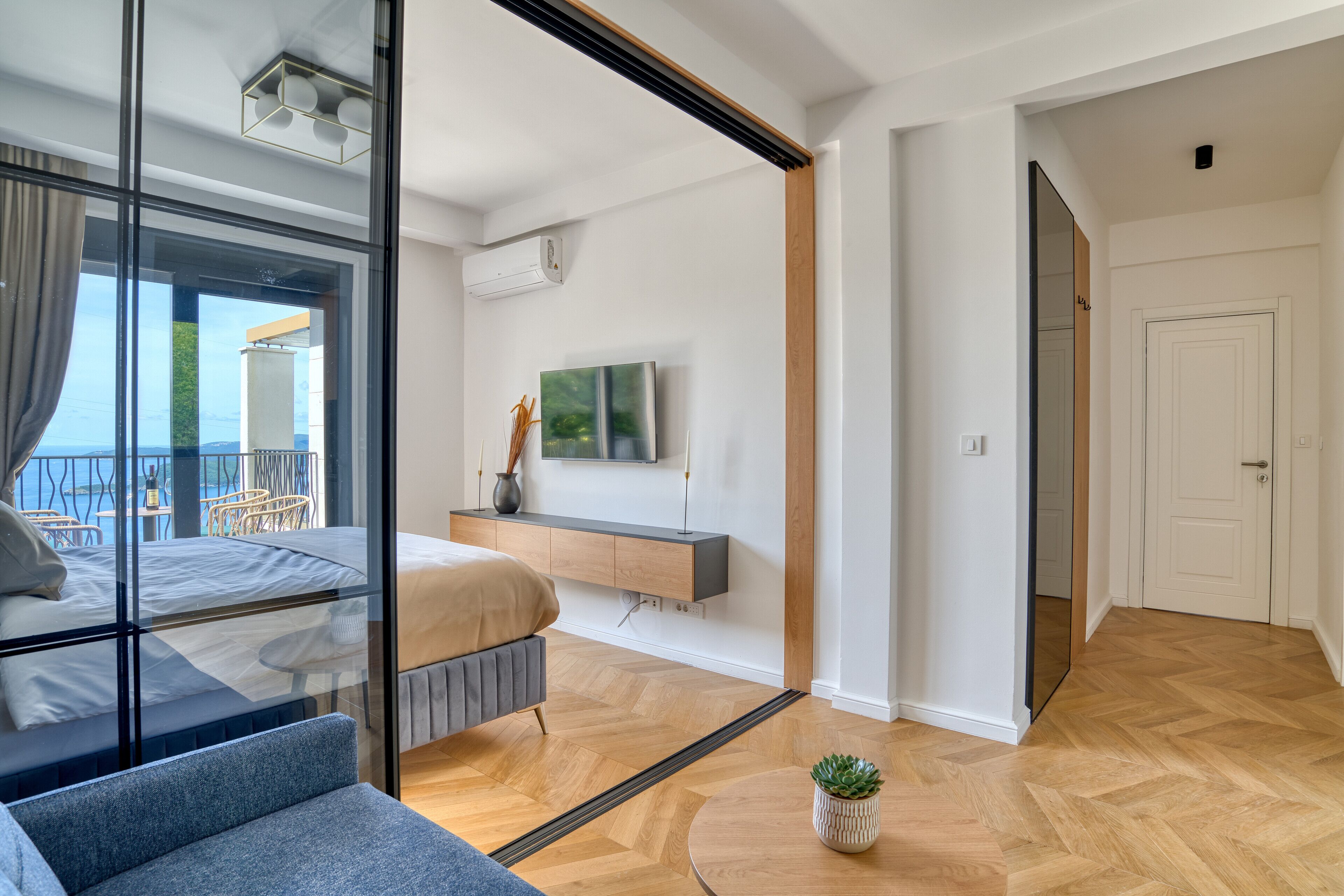 Quarto moderno com divisória de vidro, uma cama, um sofá, uma televisão e uma pequena planta.