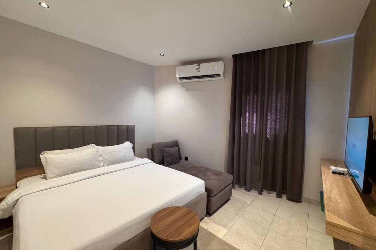 Quarto de hotel moderno com uma cama grande, um sofá pequeno, uma televisão e um aparelho de ar condicionado.