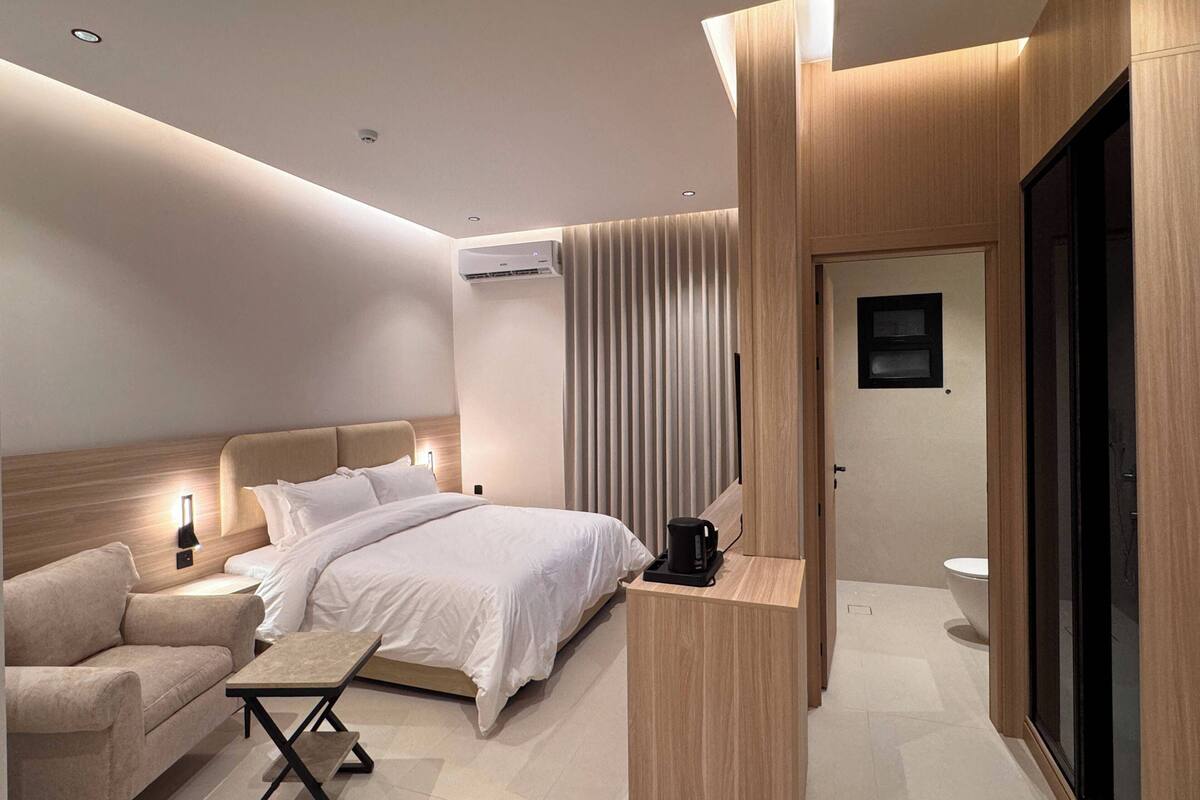 Quarto de hotel moderno com cama, mesa de cabeceira, abajur e um pequeno espaço de estar.
