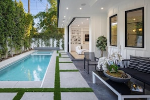 Uma área de piscina moderna ao ar livre, com vista desobstruída para a sala de estar adjacente, que inclui um sofá e uma mesa de jantar.