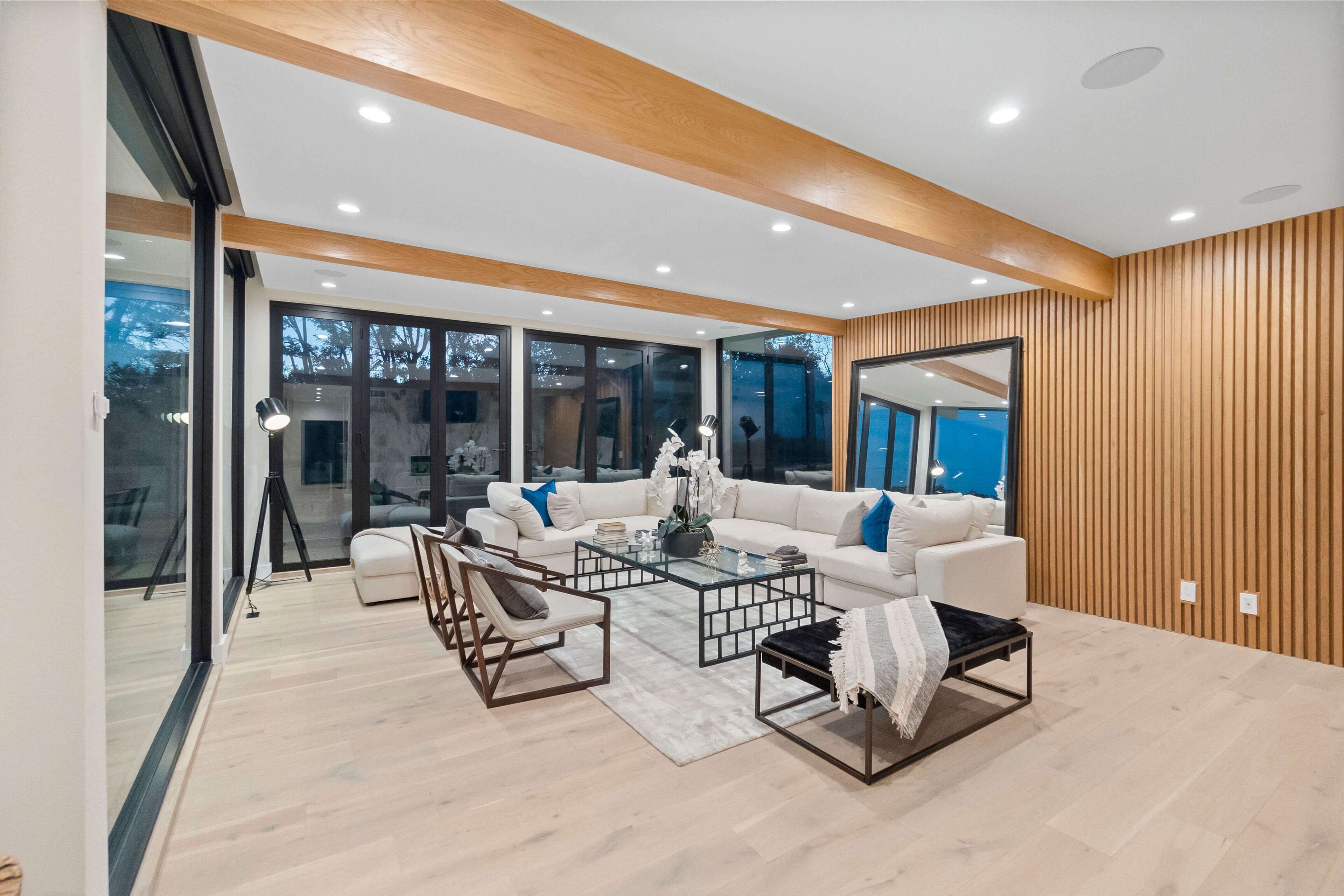 Uma sala de estar moderna com um sofá branco, uma mesa de centro de vidro e uma parede de destaque em madeira.
