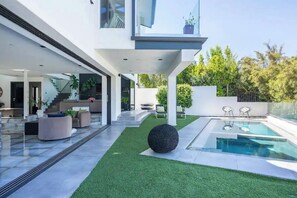 Uma casa moderna com piscina, área de estar externa e escada que leva ao andar superior.