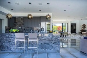 Cozinha moderna com bancadas de mármore, eletrodomésticos de aço inoxidável e iluminação pendente.