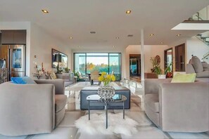 Ampla sala de estar com design moderno, com dois sofás, uma mesa de centro e uma grande janela com vista para o exterior.