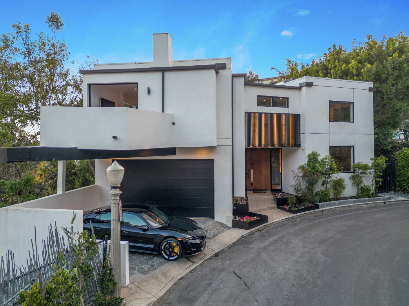 Uma casa moderna de dois andares com garagem, um carro estacionado em frente e um jardim bem cuidado.