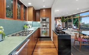 Uma cozinha moderna com armários de madeira, eletrodomésticos de aço inoxidável e uma grande janela com vista para um jardim.