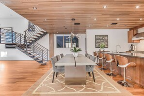 Uma área de refeições moderna com uma mesa comprida, banquetas de bar e uma escada.