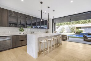 Cozinha moderna com bancada de mármore, armários de madeira e área de bar com banquetas.