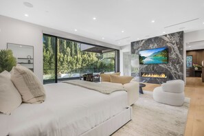 Quarto moderno com uma cama grande, televisão fixada em uma parede de mármore e lareira.