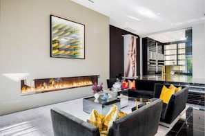 Uma sala de estar moderna com lareira, um grande quadro abstrato e um espaço de estar com uma mesa de centro de vidro.
