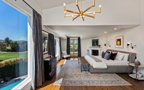 Quarto moderno com uma grande janela, um candelabro, uma lareira e vista para um campo de golfe.