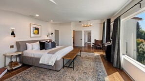 Quarto moderno com uma cama grande, um banquinho, um tapete e vista para o exterior.