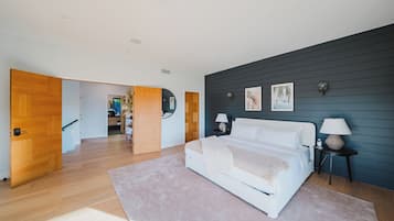 Quarto moderno com uma cama grande, mesas de cabeceira e vista para outro espaço.