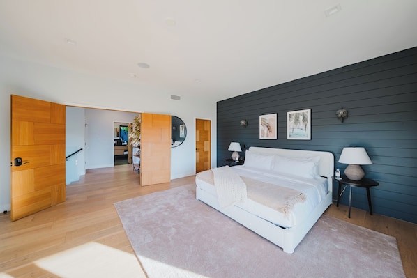 Quarto moderno com uma cama grande, mesas de cabeceira e vista para outro espaço.
