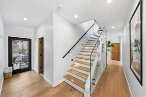 Um interior moderno com escada de madeira, paredes brancas e porta de vidro que dá para uma área externa.