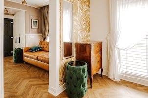 Um quarto com um sofá, um banquinho verde, um armário de madeira e uma janela com cortinas.