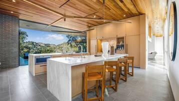 Cozinha moderna com uma ilha grande, cadeiras de madeira e vista para uma paisagem montanhosa.