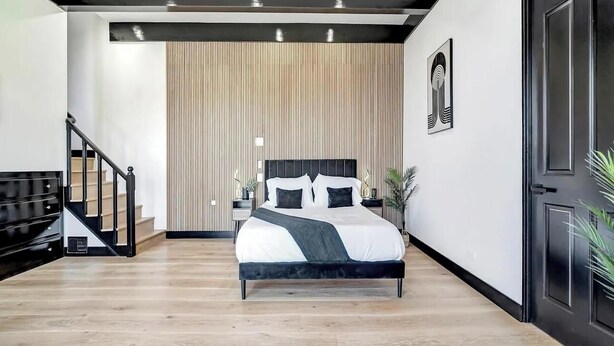Quarto moderno com uma cama grande, uma parede de ripas de madeira, uma escada e uma porta preta.
