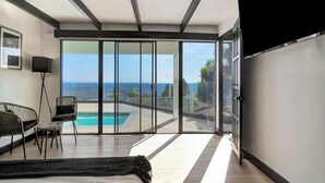 Quarto com cama grande, escrivaninha, cadeira e vista para uma piscina e oceano.