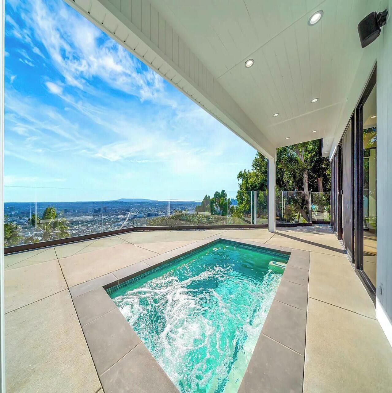 Piscina moderna ao ar livre com vista para a cidade, rodeada por um terraço coberto.