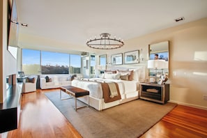 Um quarto espaçoso com uma cama grande, um espaço de estar com sofá, uma mesa de jantar e vista para o exterior.