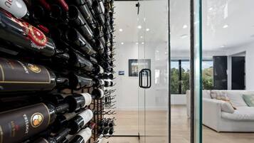 Uma adega com garrafas de vinho, uma porta de vidro que dá para um espaço com sofá branco e vista para o verde lá fora.
