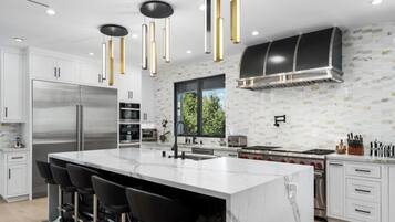 Cozinha moderna com uma ilha grande, eletrodomésticos de aço inoxidável e iluminação pendente.