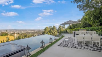 Piscina infinita no terraço com vista para a cidade, área de estar externa e piso estampado.