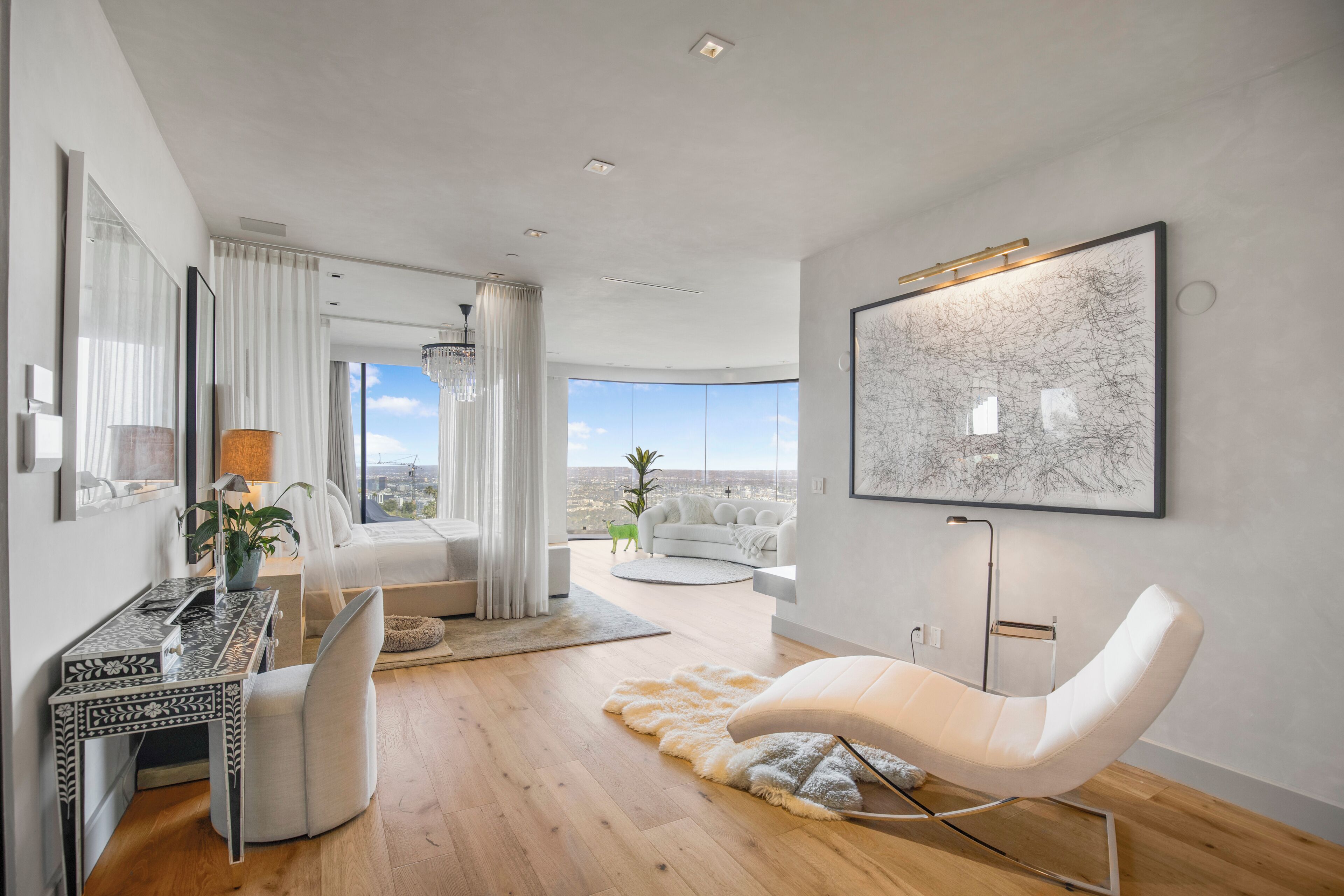 Uma sala de estar moderna com um sofá branco, uma poltrona branca, uma escrivaninha e um grande quadro abstrato na parede.