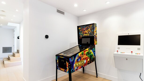 Quarto com mesa de console de jogos, parede branca e escada.