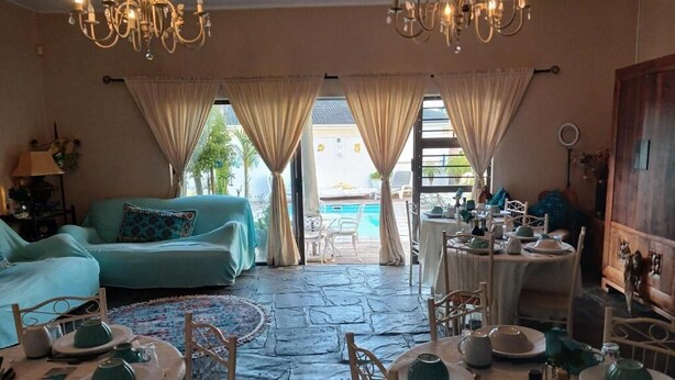 Uma sala de jantar com piso de pedra, uma mesa redonda posta para refeição e vista para uma piscina externa.