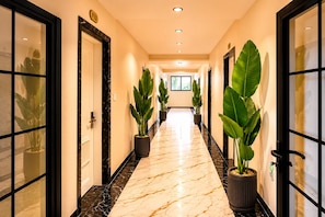 Corredor de hotel com piso de mármore, plantas em vasos e portas com painéis de vidro.