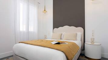 Quarto com cama, mesas de cabeceira e janela com cortinas leves.