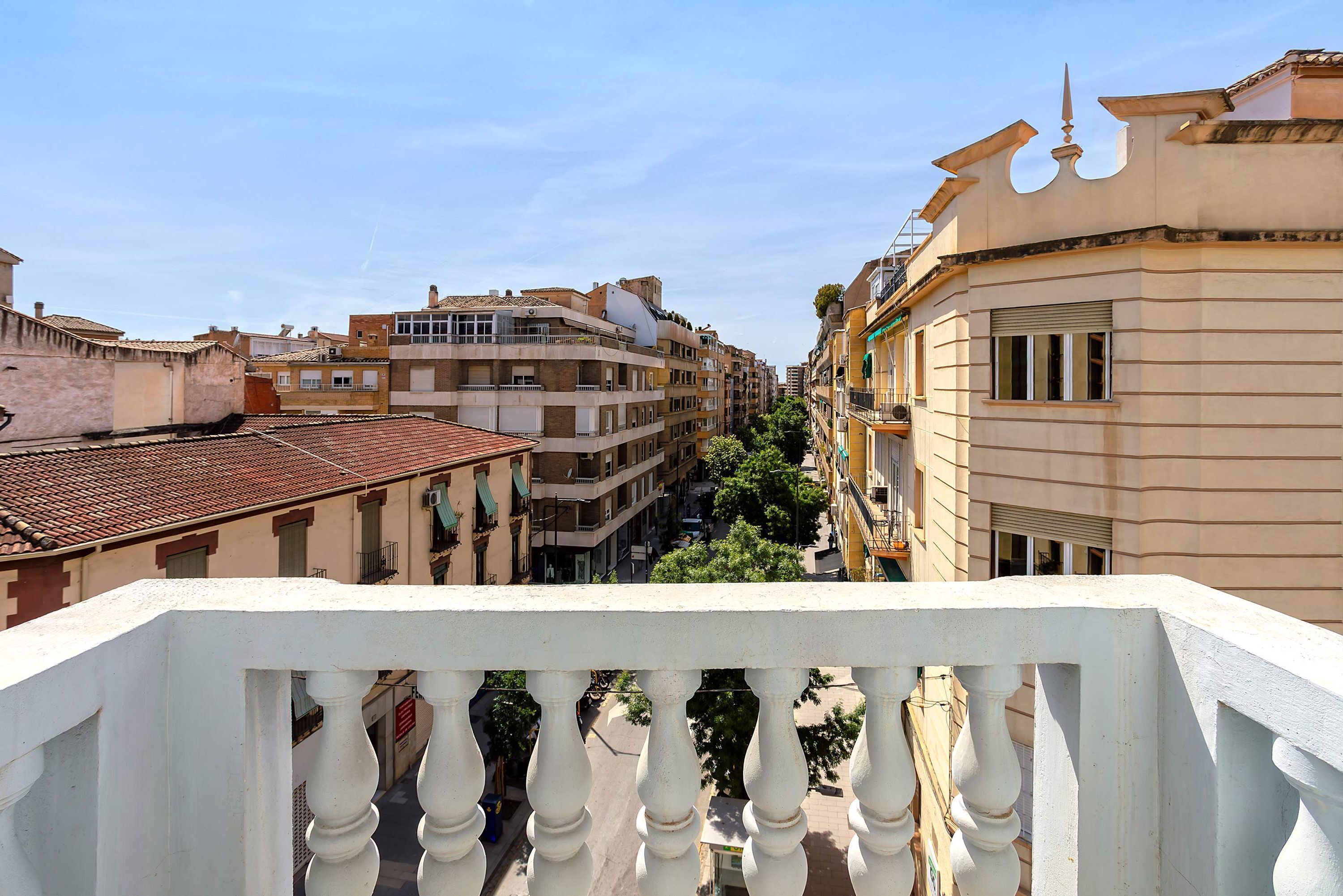Vista de uma varanda com vista para uma rua estreita, ladeada por edifícios altos com varandas e diferentes estilos arquitetônicos.