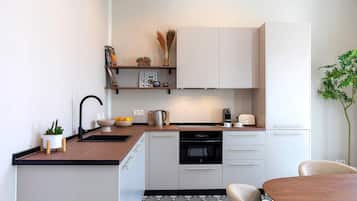 Uma cozinha moderna com armários brancos, bancada de madeira, forno embutido e um espaço de refeições com mesa e cadeiras redondas.